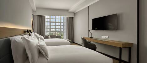 Quarto de hotel moderno com duas camas, TV, escrivaninha e vista para a cidade.
