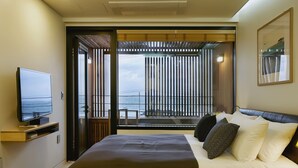 Quarto de hotel com cama, televisão, varanda com vista para o mar e um painel de madeira.