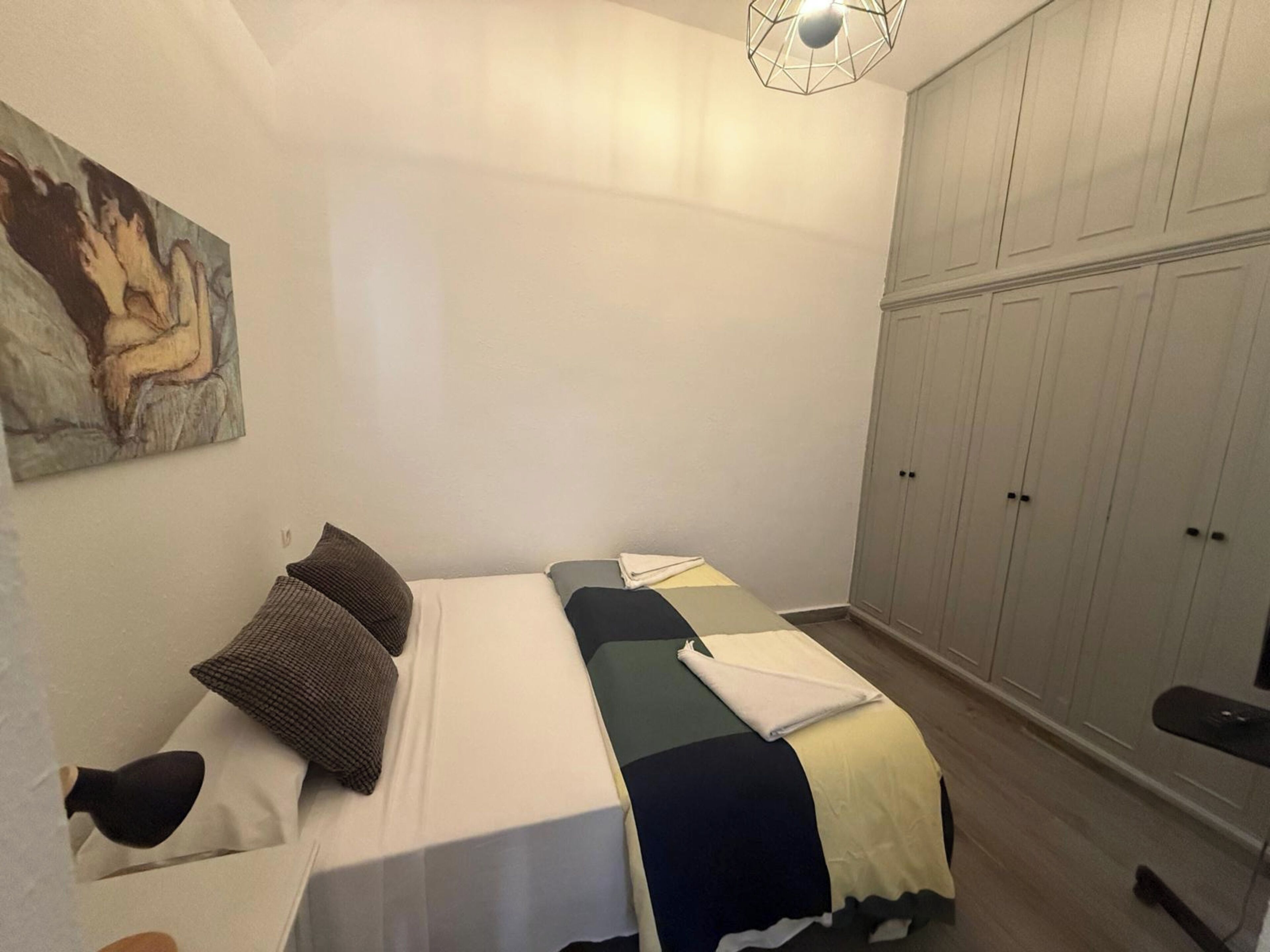 Quarto com cama, travesseiros, cobertor, escrivaninha e guarda-roupa.