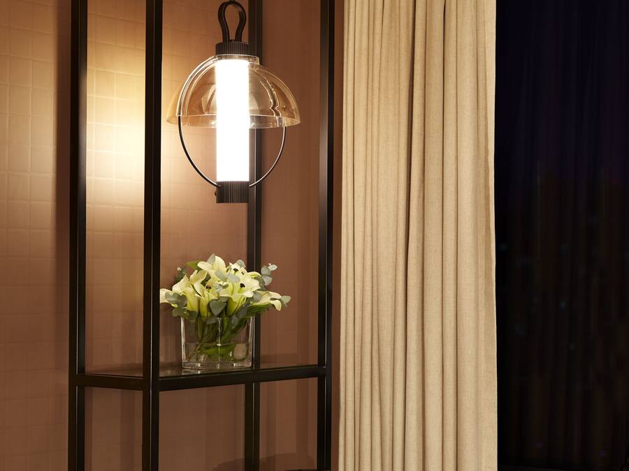 Quarto moderno com um armário de madeira, um vaso de vidro com flores, uma cafeteira e um candeeiro suspenso.