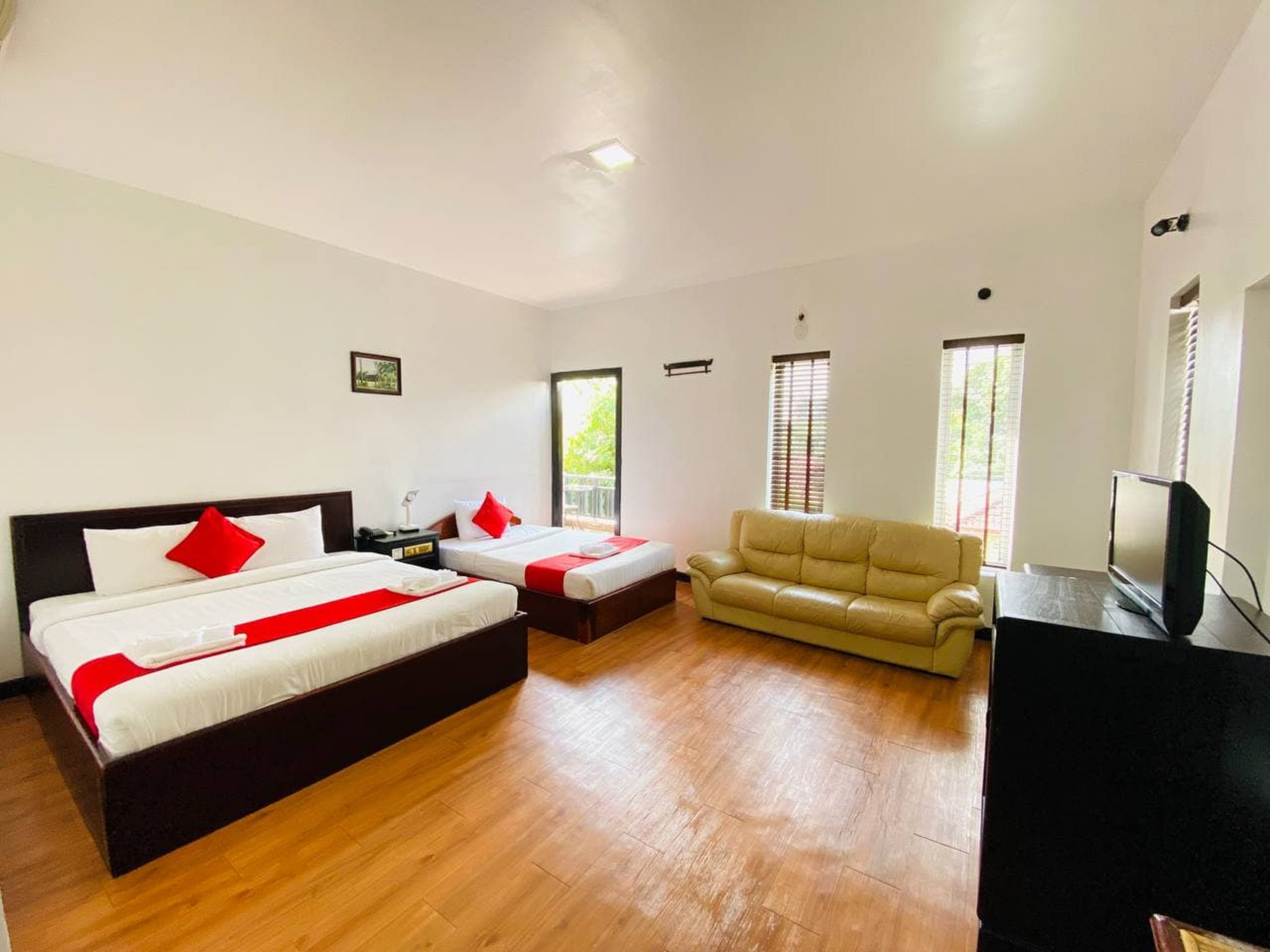 Quarto de hotel com duas camas, um sofá, uma TV e janelas amplas.