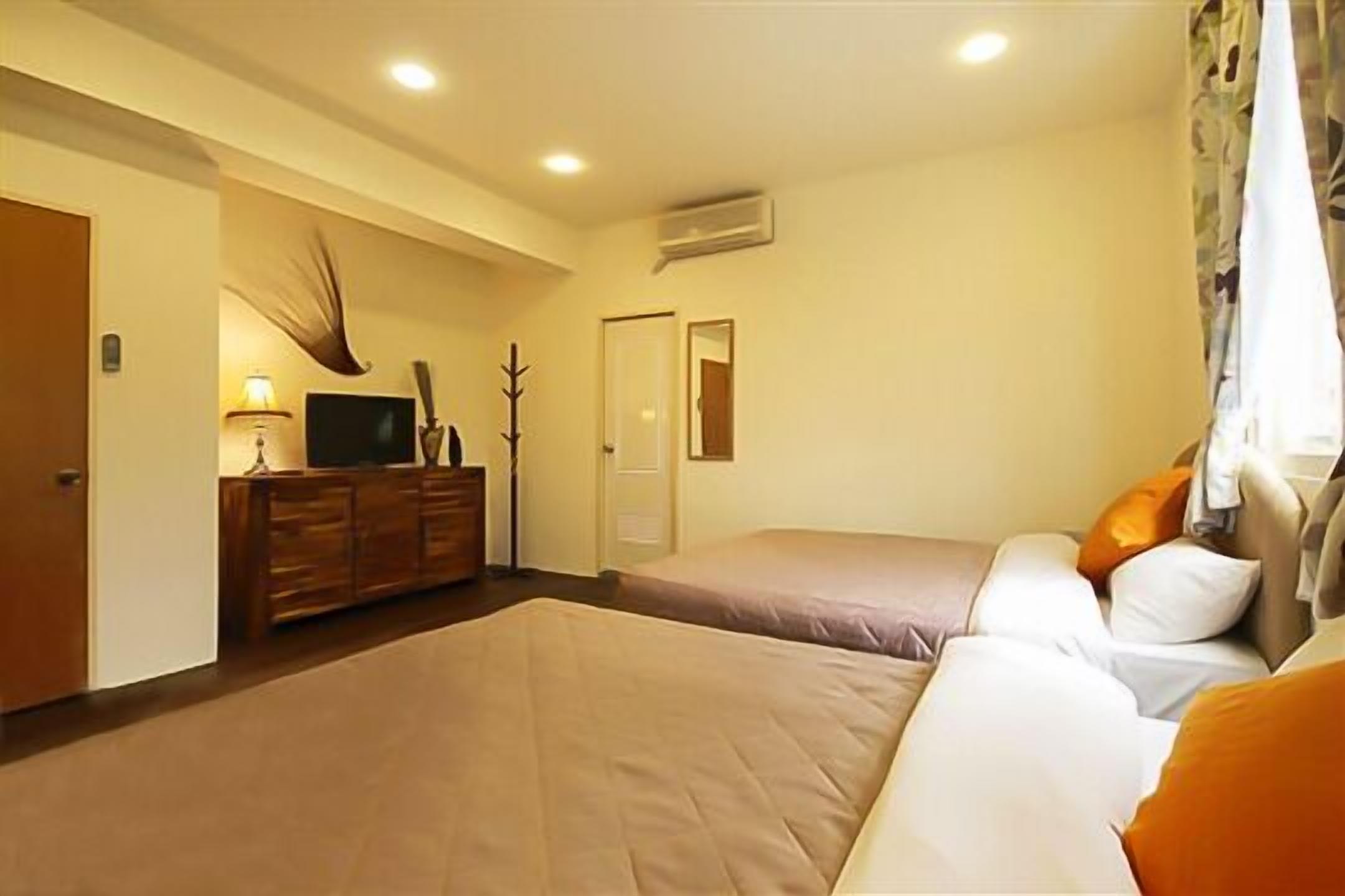 Quarto de hotel com duas camas, uma cômoda, uma televisão e um espelho.