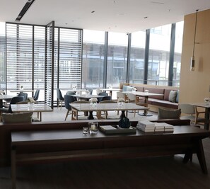 Espaço lounge moderno com disposição de assentos, mesas e amplas janelas oferecendo vistas.