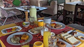 Uma área de refeições ao ar livre com uma mesa posta para o café da manhã, incluindo pratos de comida, bebidas e diversas opções para o café.