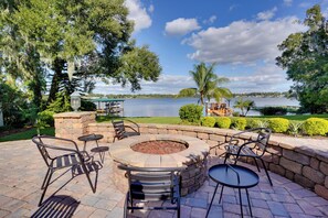 Um pátio com móveis de exterior, lareira e vista para um lago.