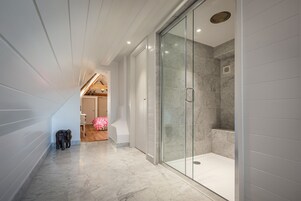 Casa de banho moderna com cabine de duche em vidro, soalho em mármore e porta visível para outro espaço.