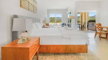 Quarto de hotel moderno com uma cama grande, mesa de cabeceira de madeira, escrivaninha e varanda com vista para as colinas.