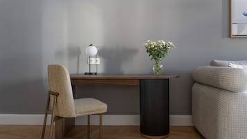 Quarto moderno com escrivaninha de madeira, uma cadeira, uma mesinha com um vaso de flores e um sofá.