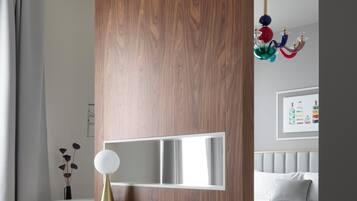 Quarto moderno com divisória de madeira, escrivaninha com cadeira, cama com cabeceira cinza e lustre.