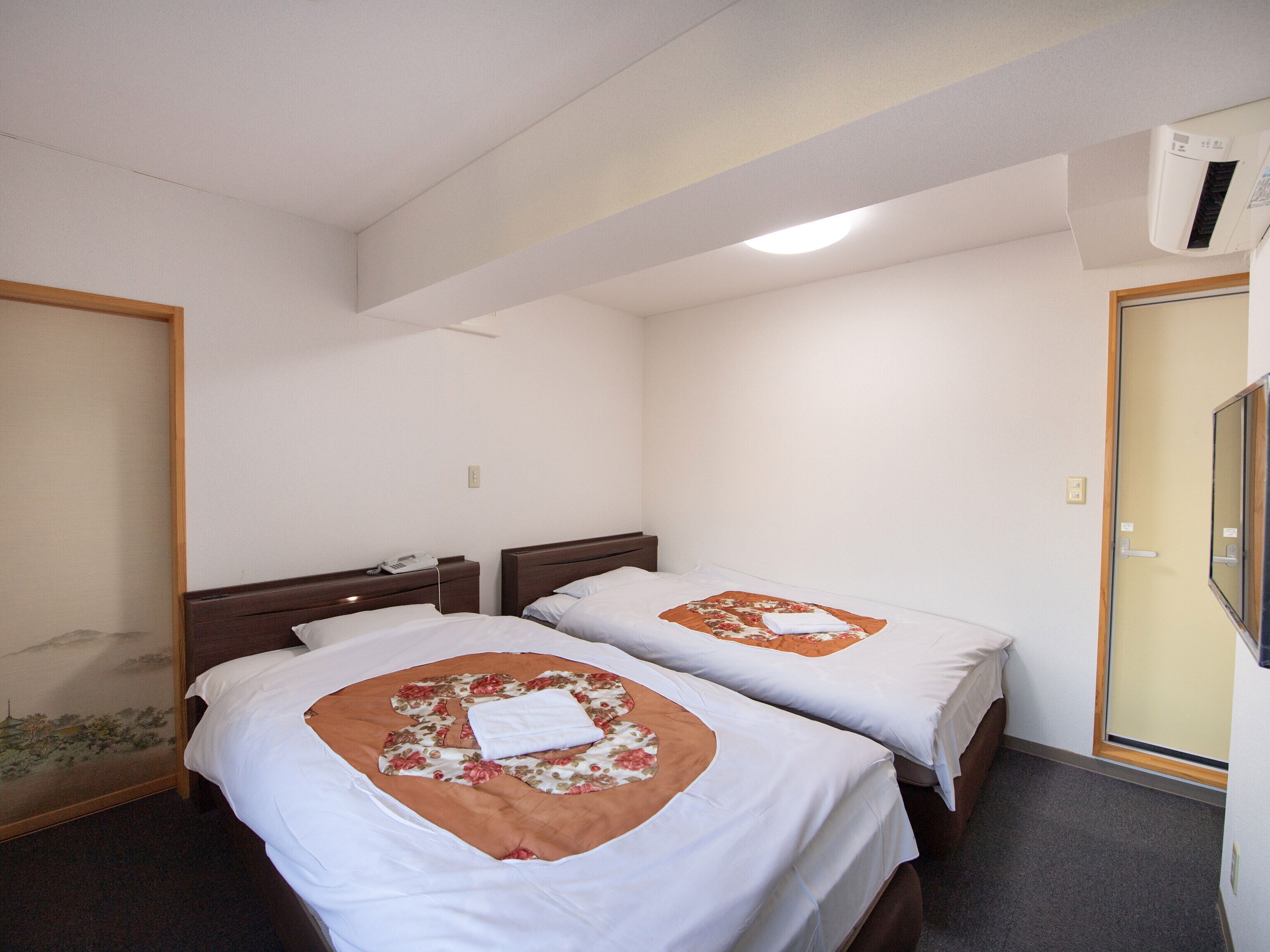 Quarto de hotel com duas camas, cabeceira de madeira, ar condicionado fixado na parede e uma porta com espelho.