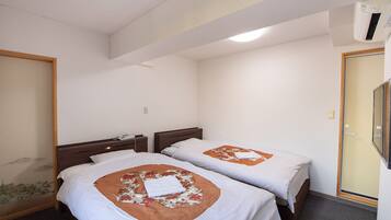 Quarto de hotel com duas camas, cabeceira de madeira, ar condicionado fixado na parede e uma porta com espelho.