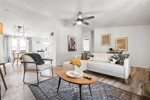 Uma sala de estar moderna com um sofá branco, uma mesa de centro e um ventilador de teto.