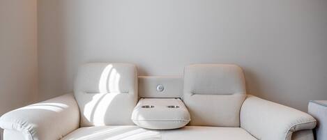 Uma sala de estar moderna e minimalista, com um sofá branco, uma mesinha lateral e um comedouro para animais de estimação embutido.