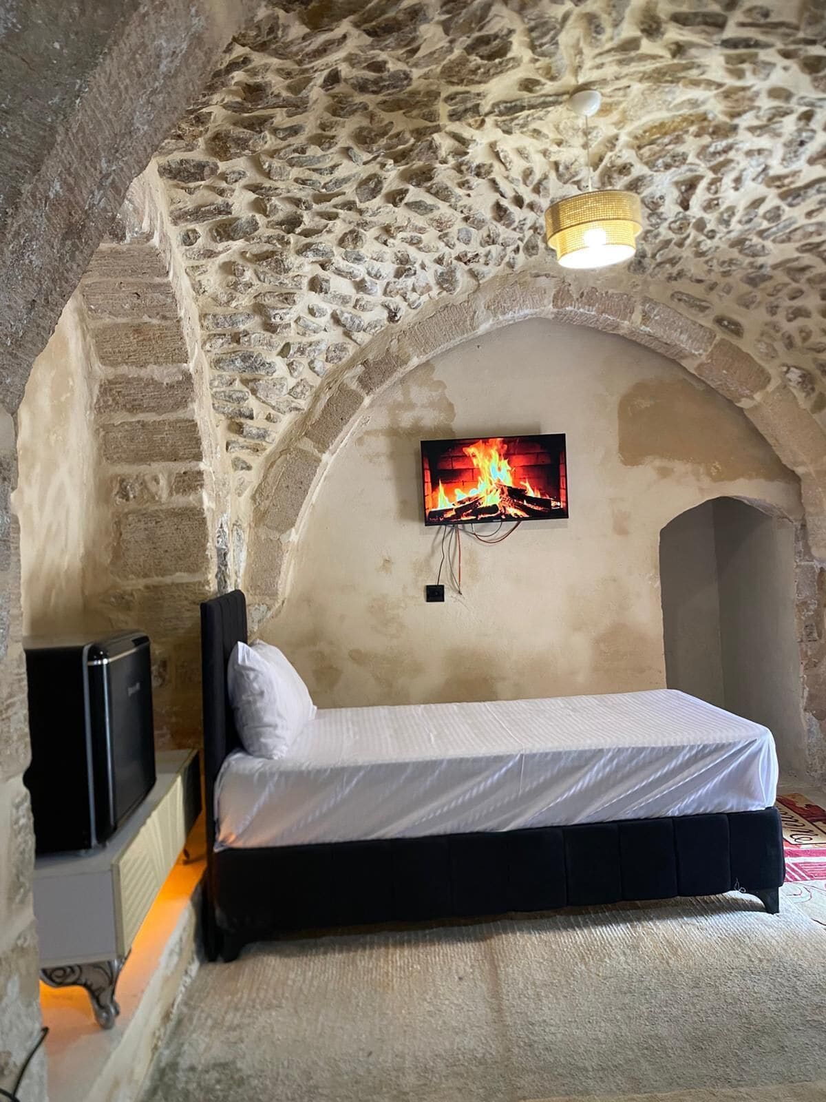 Quarto com teto de pedra, uma cama, televisão e lareira.
