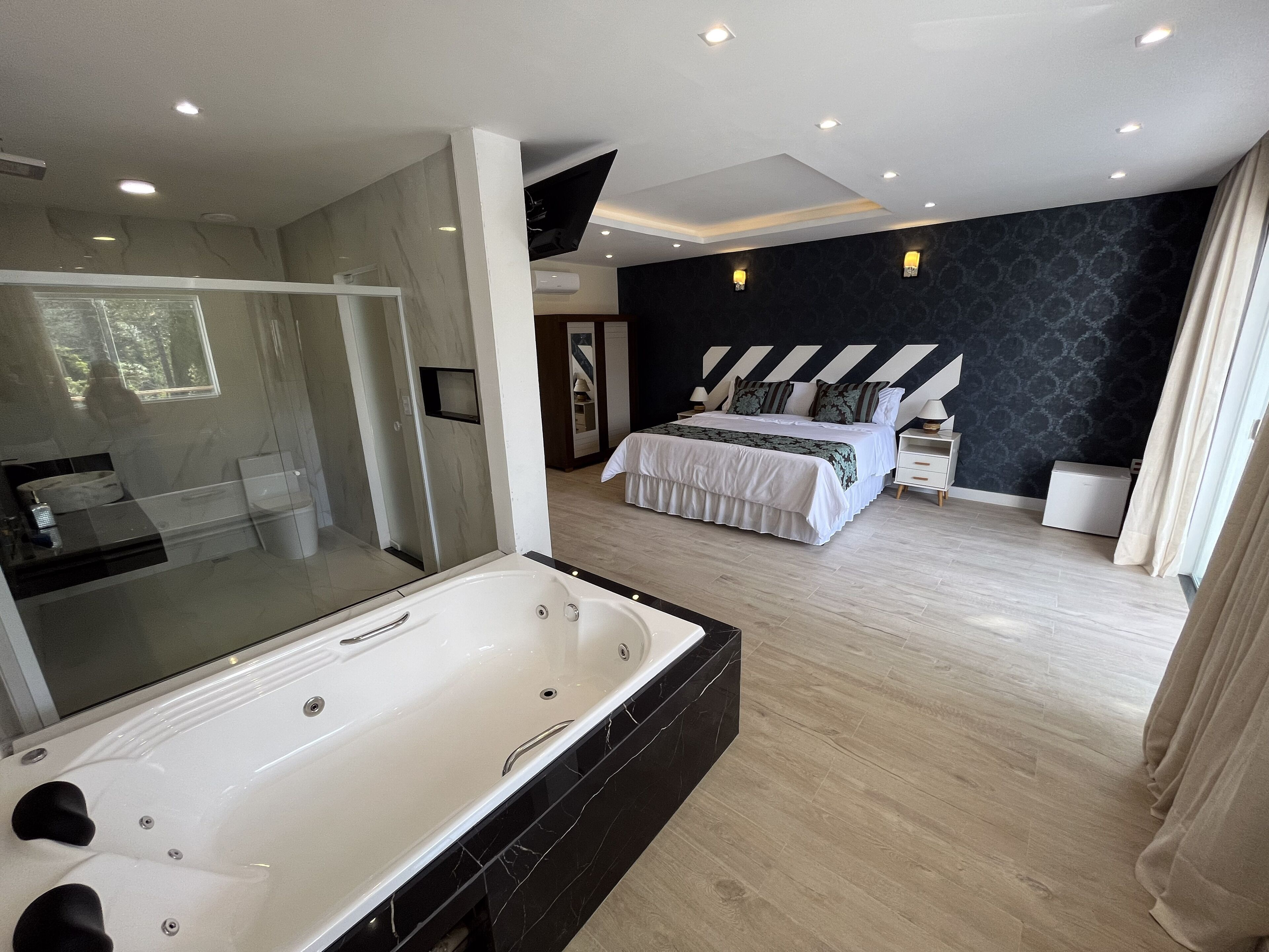 Quarto moderno com cama grande, banheiro separado com banheira e closet espaçoso.