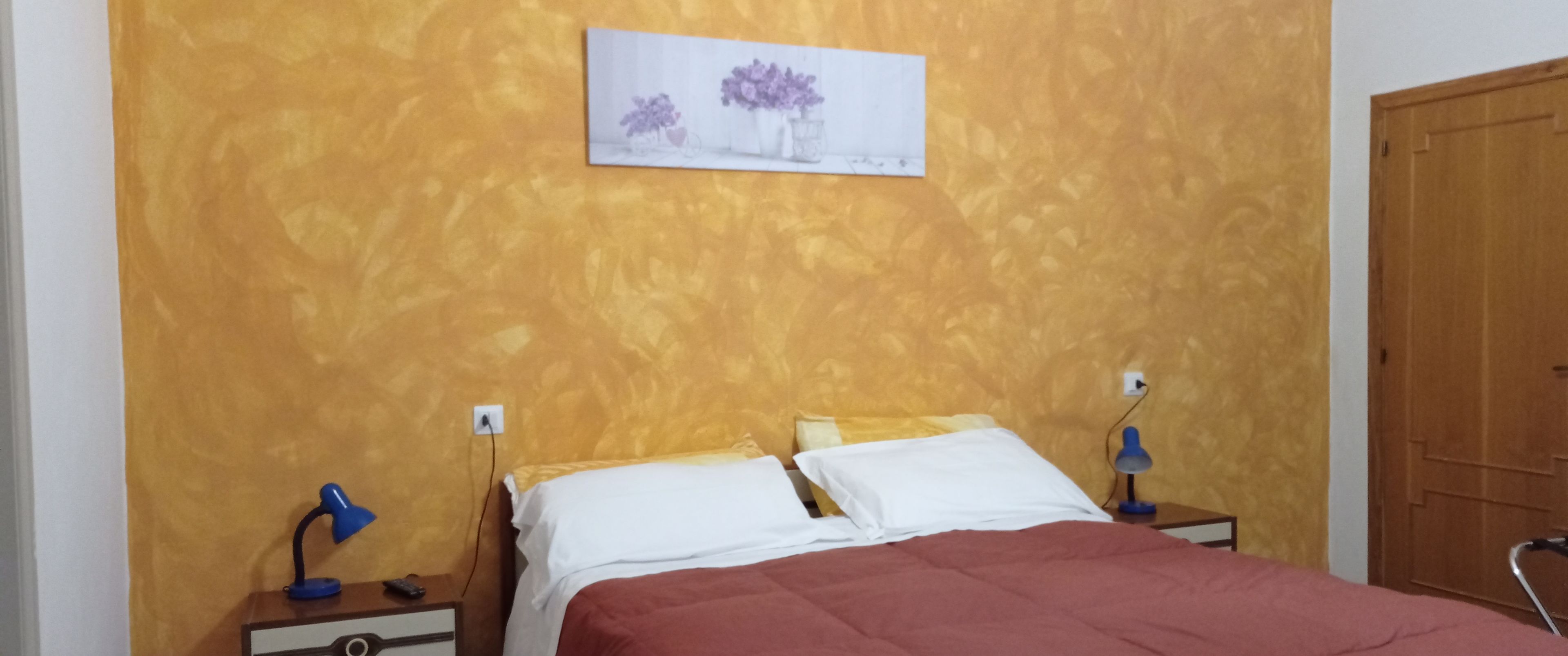 Quarto com cama, duas mesas de cabeceira, abajur, quadro na parede e guarda-roupa de madeira.