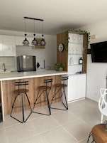 Cozinha moderna com ilha central, banquetas, geladeira e televisão fixada na parede.