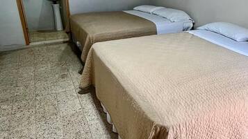Quarto pequeno e simples com duas camas, uma pia e um espelho.