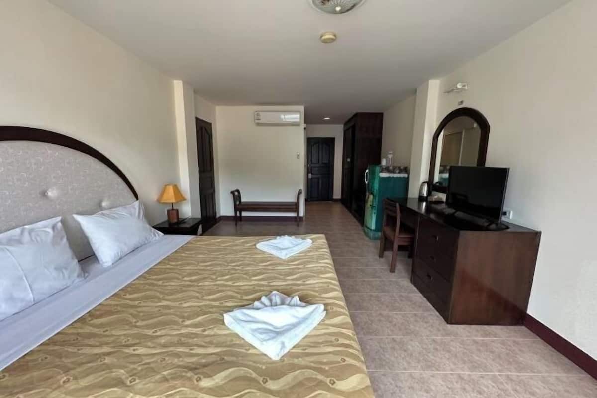 Quarto de hotel com cama, escrivaninha, televisão e espelho.