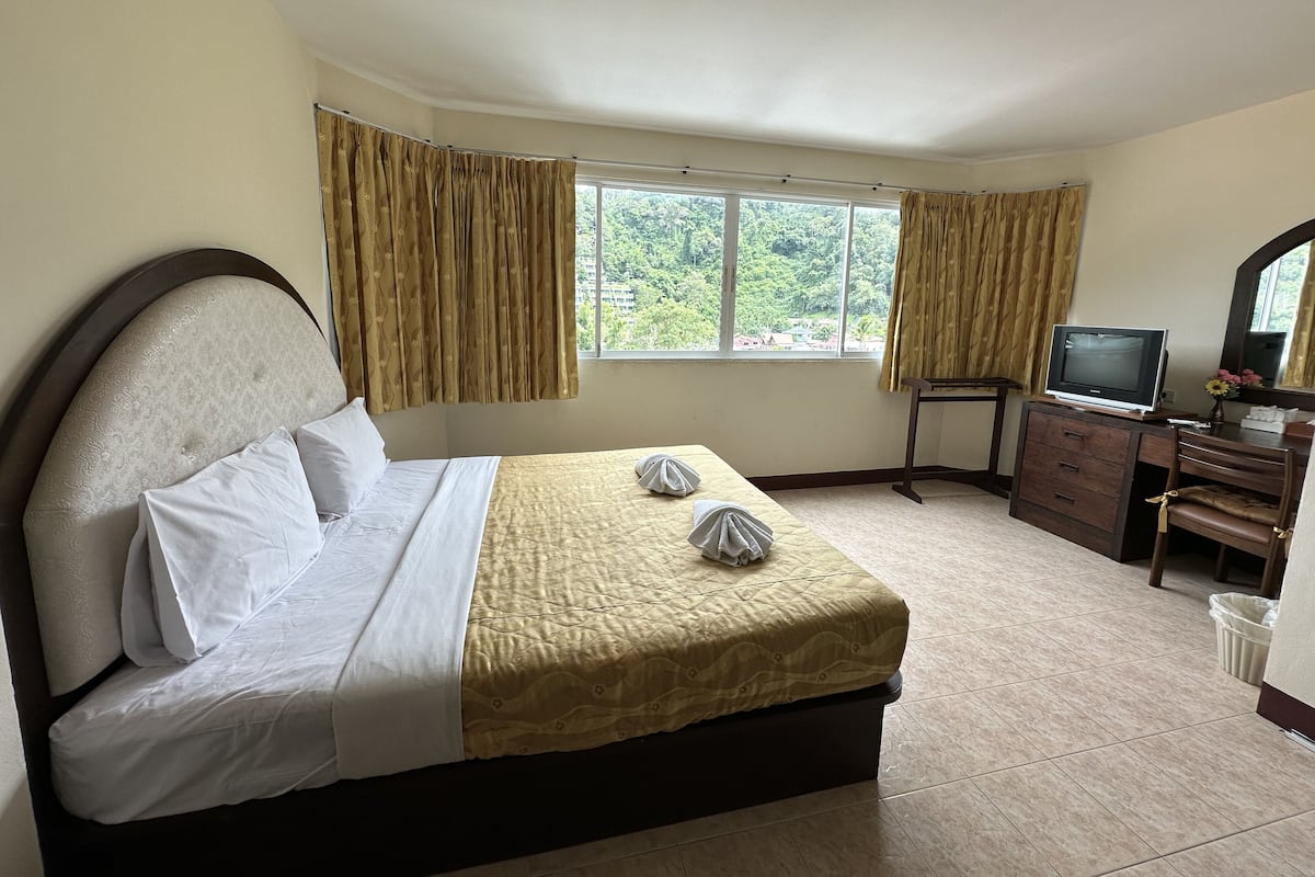 Quarto de hotel com cama, escrivaninha com televisão e janela com cortinas.