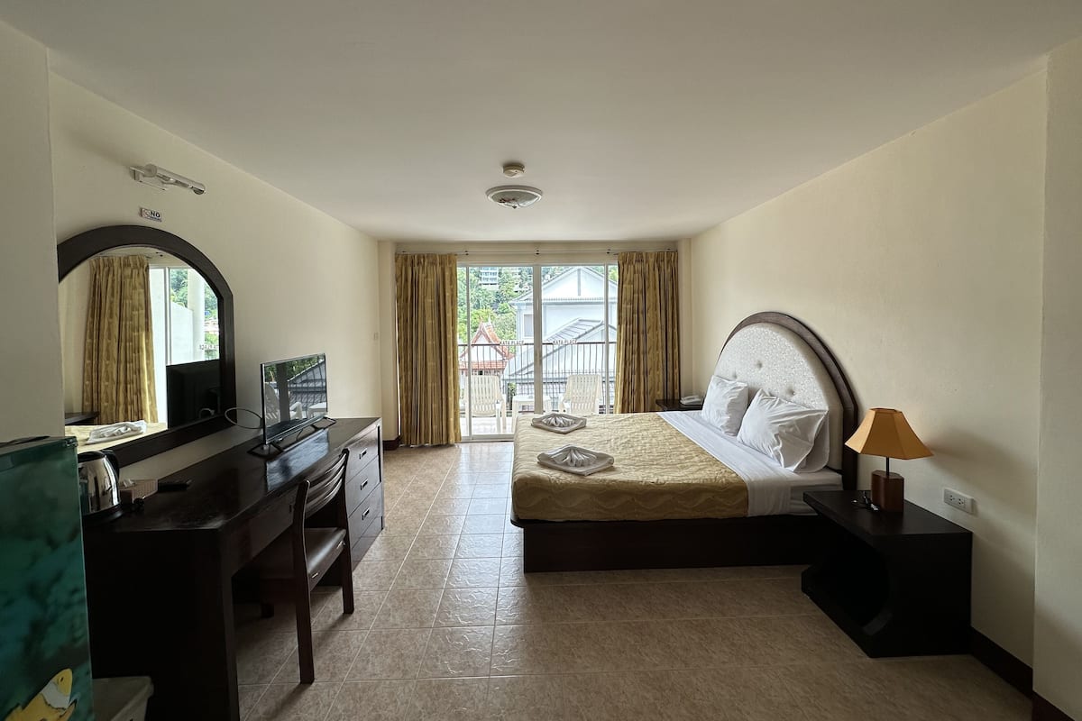 Quarto de hotel com cama, escrivaninha, cadeira, televisão e vista para o exterior.