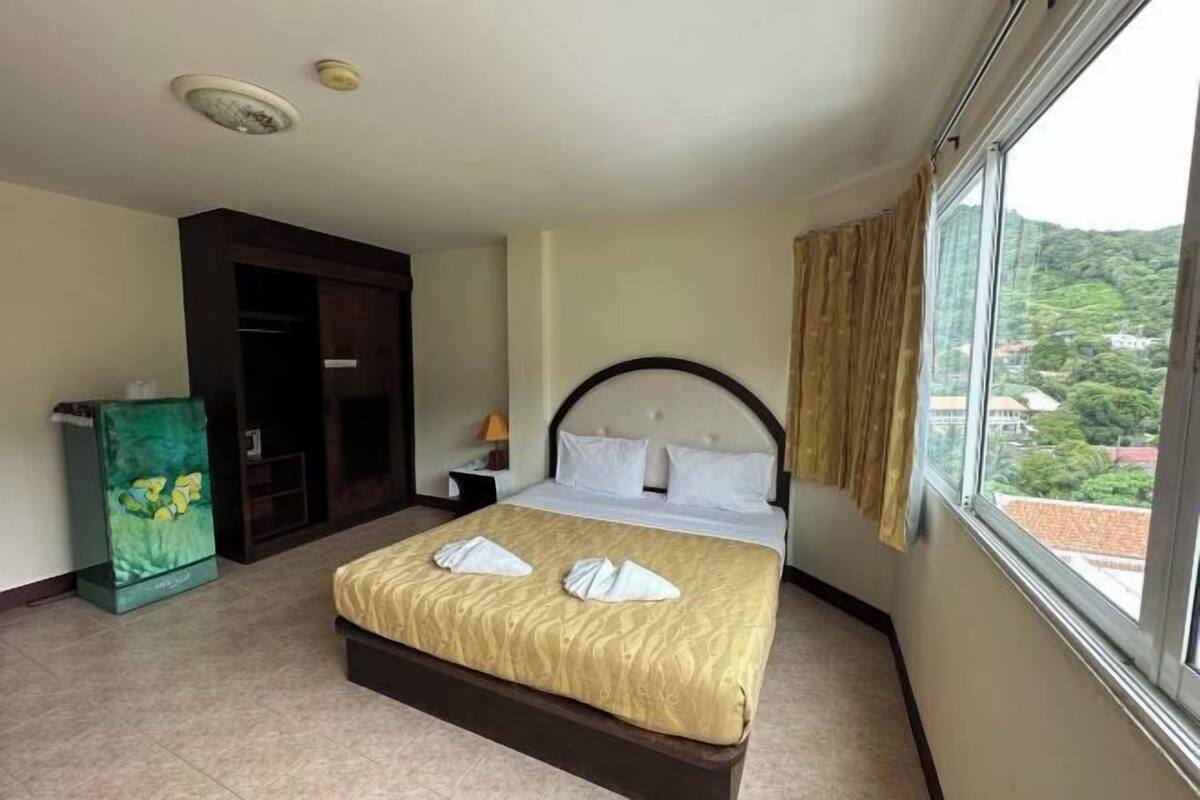 Quarto de hotel com cama, guarda-roupa, um armário verde e janela com vista para vegetação.