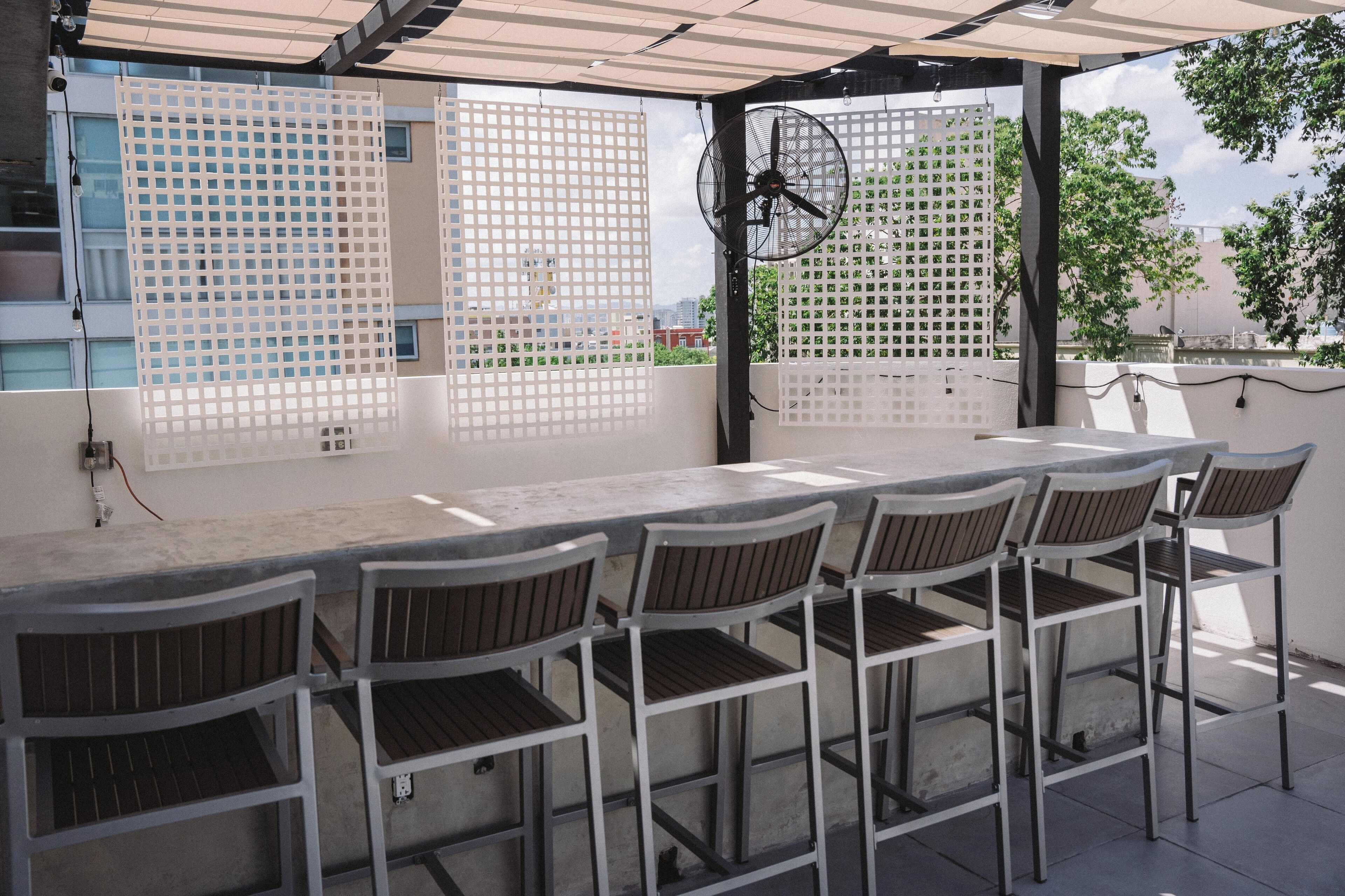 Pátio externo com uma mesa comprida e seis cadeiras, cercado por uma cerca de treliça branca.
