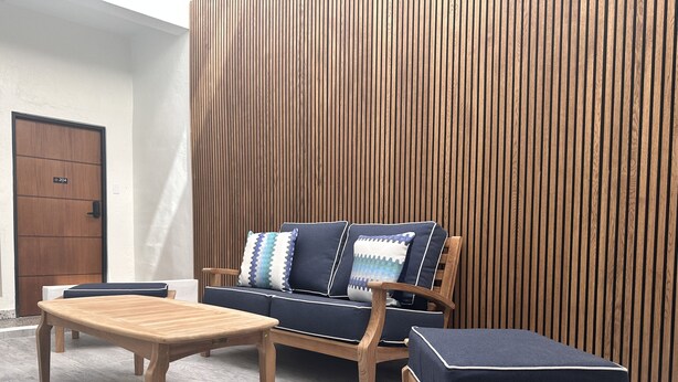 Uma área de estar moderna ao ar livre, com uma mesa de madeira e duas cadeiras estofadas, um banco de madeira e um painel de parede de madeira vertical.