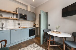 Uma cozinha moderna com armários azul claro, micro-ondas e forno embutido. Há um espaço de refeições com uma mesa redonda e duas cadeiras.