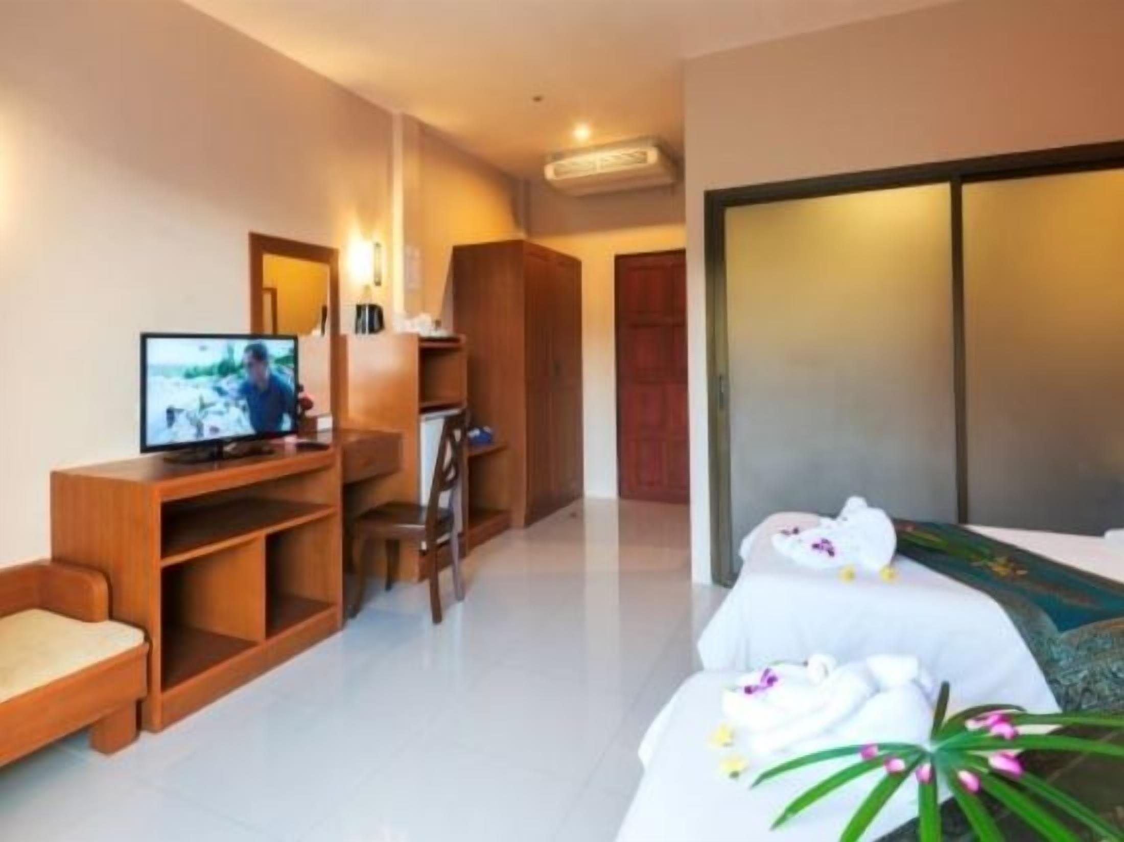 Quarto de hotel com cama, televisão, área de estar e guarda-roupa.