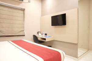 Quarto de hotel com cama, escrivaninha e cadeira, televisão de tela plana na parede e janela com persianas.