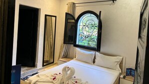 Quarto de hotel com uma cama, uma janela com design decorativo, um espelho e uma mesa de cabeceira.