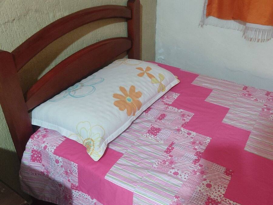 Cama com colcha rosa e travesseiro branco estampado com motivos florais.