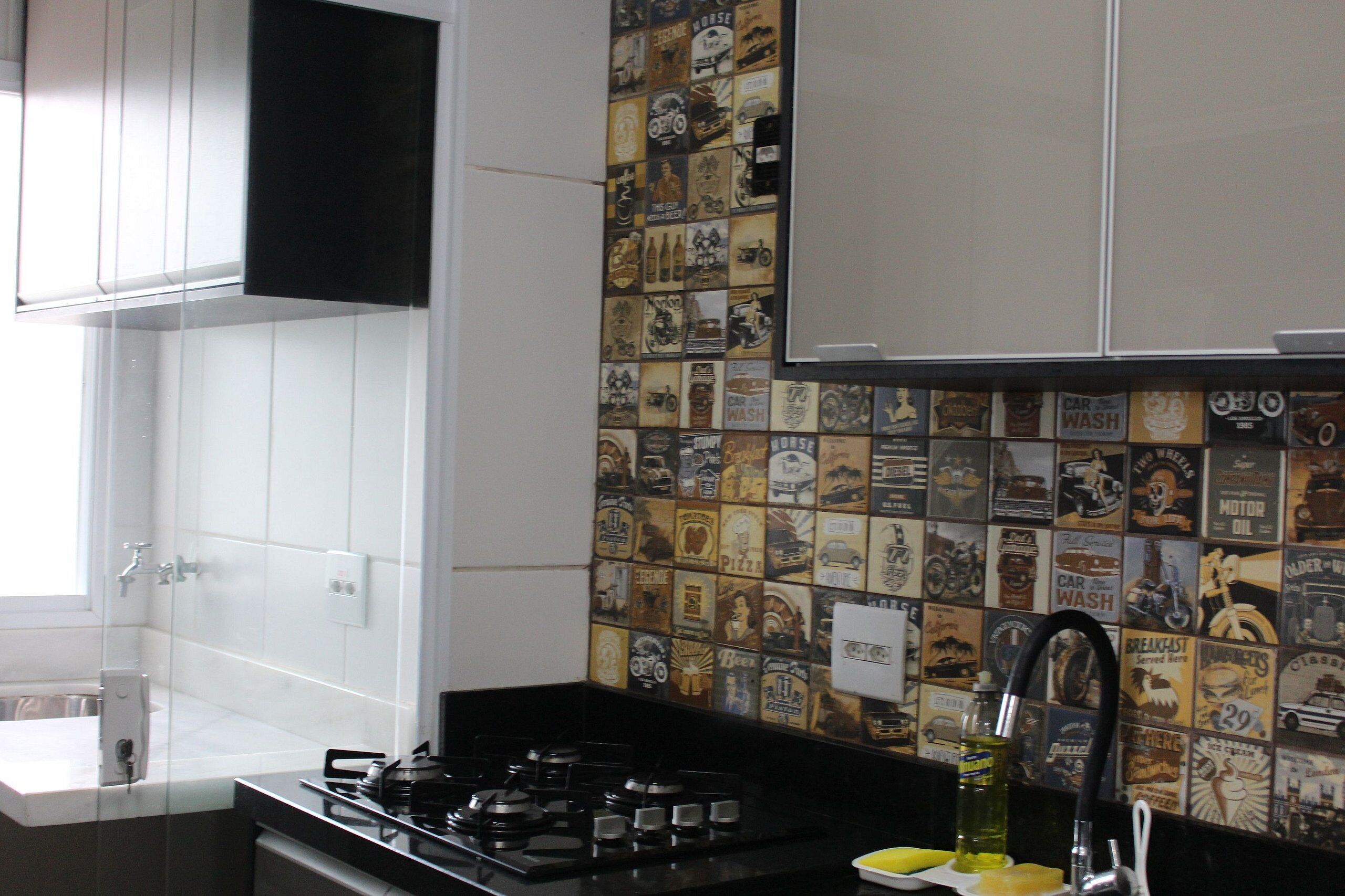 Cozinha com fogão preto, armários brancos e painel decorado com azulejos de carros e motocicletas antigos.