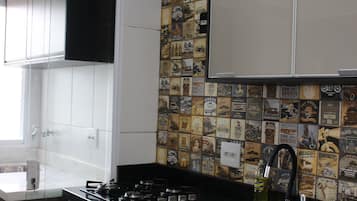 Cozinha com fogão preto, armários brancos e painel decorado com azulejos de carros e motocicletas antigos.