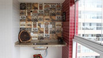 Cozinha com painel de azulejos com desenhos de automóveis antigos, uma pia de aço inoxidável e uma janela com vista para um edifício.