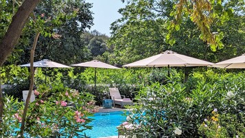 Uma área de piscina com espreguiçadeiras e guarda-sóis, cercada por vegetação exuberante e plantas floridas.