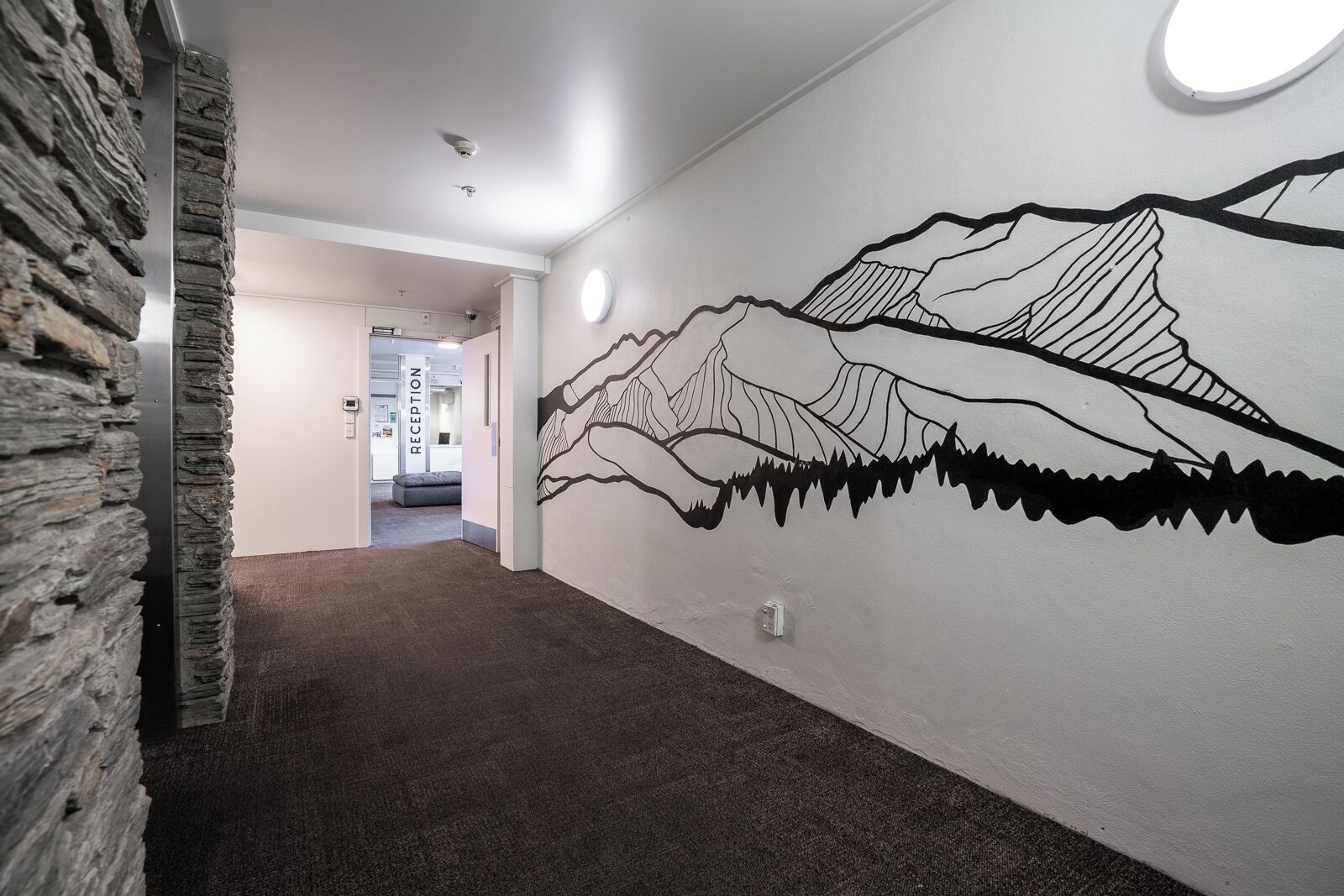 Um corredor com uma parede de pedra de um lado e um mural de montanhas do outro.