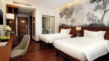 Quarto de hotel com duas camas, uma escrivaninha com cadeira, um vaso de flores e um mural grande na parede.