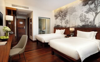 Quarto de hotel com duas camas, uma escrivaninha com cadeira, um vaso de flores e um mural grande na parede.