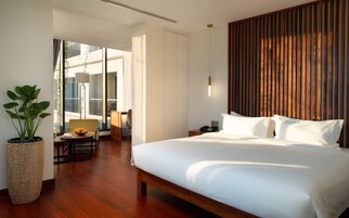 Quarto de hotel moderno com uma cama grande, parede de ripas de madeira, planta em vaso e varanda com vista.