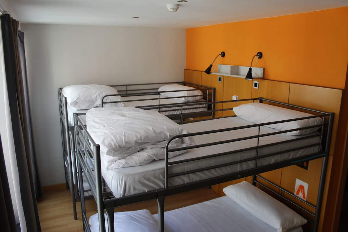 Quarto de dormitório com beliches, prateleira na parede e luminária no teto.