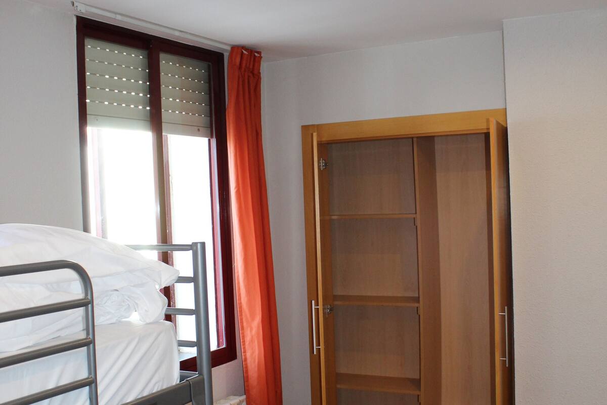 Quarto com beliche, guarda-roupa de madeira e janela com cortinas.