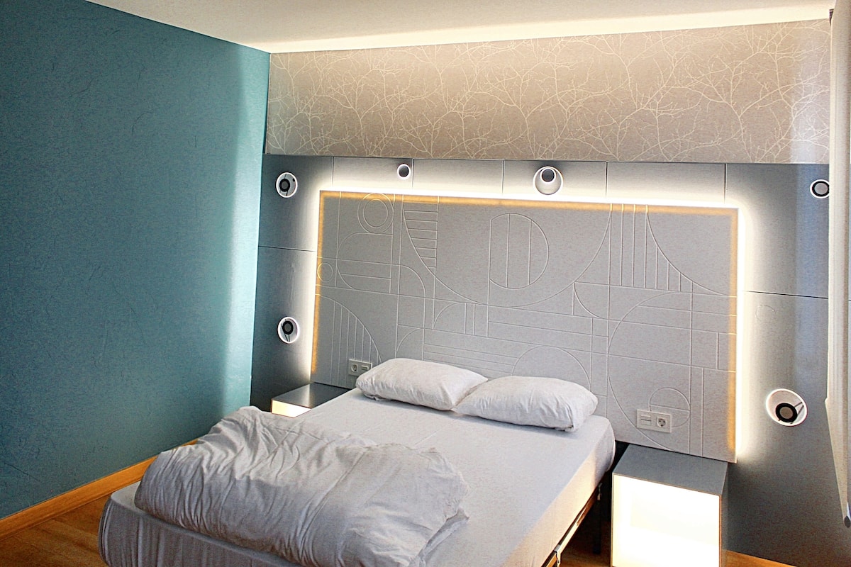 Quarto moderno com uma cama grande, duas mesas de cabeceira e uma cabeceira com iluminação embutida.