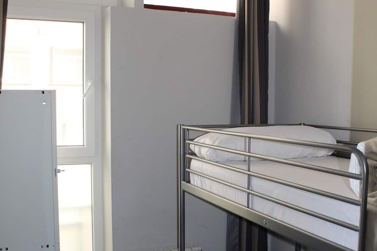 Uma cama de solteiro com roupa de cama branca, uma mesa de madeira e um radiador.