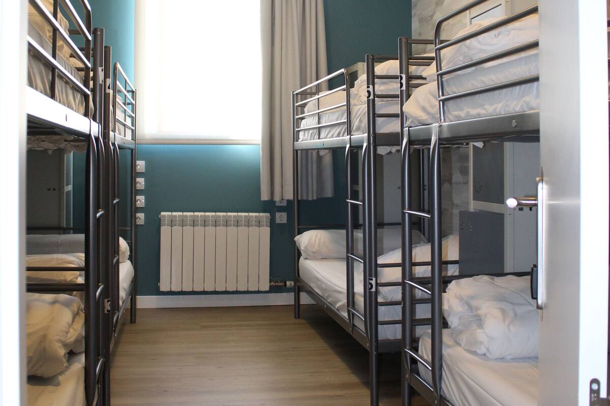 Um corredor estreito com beliches em ambos os lados, um radiador e uma janela com cortinas.