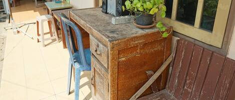 Um banco de madeira rústico com uma planta em vaso, uma cadeira de plástico azul e uma pequena mesa com uma câmera antiga e alto-falantes.