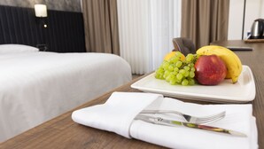 Quarto de hotel bem arrumado com uma cama, mesa de cabeceira com uma tábua de frutas e uma luminária.