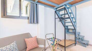 Quarto com sofá, uma mesinha com um vaso, uma cadeira de metal e uma escada azul.