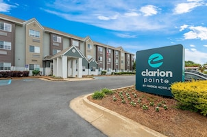 Entrada de hotel com uma placa indicando 'Clarion Pointe by Choice Hotels', um acesso por meio de um caminho e um estacionamento.